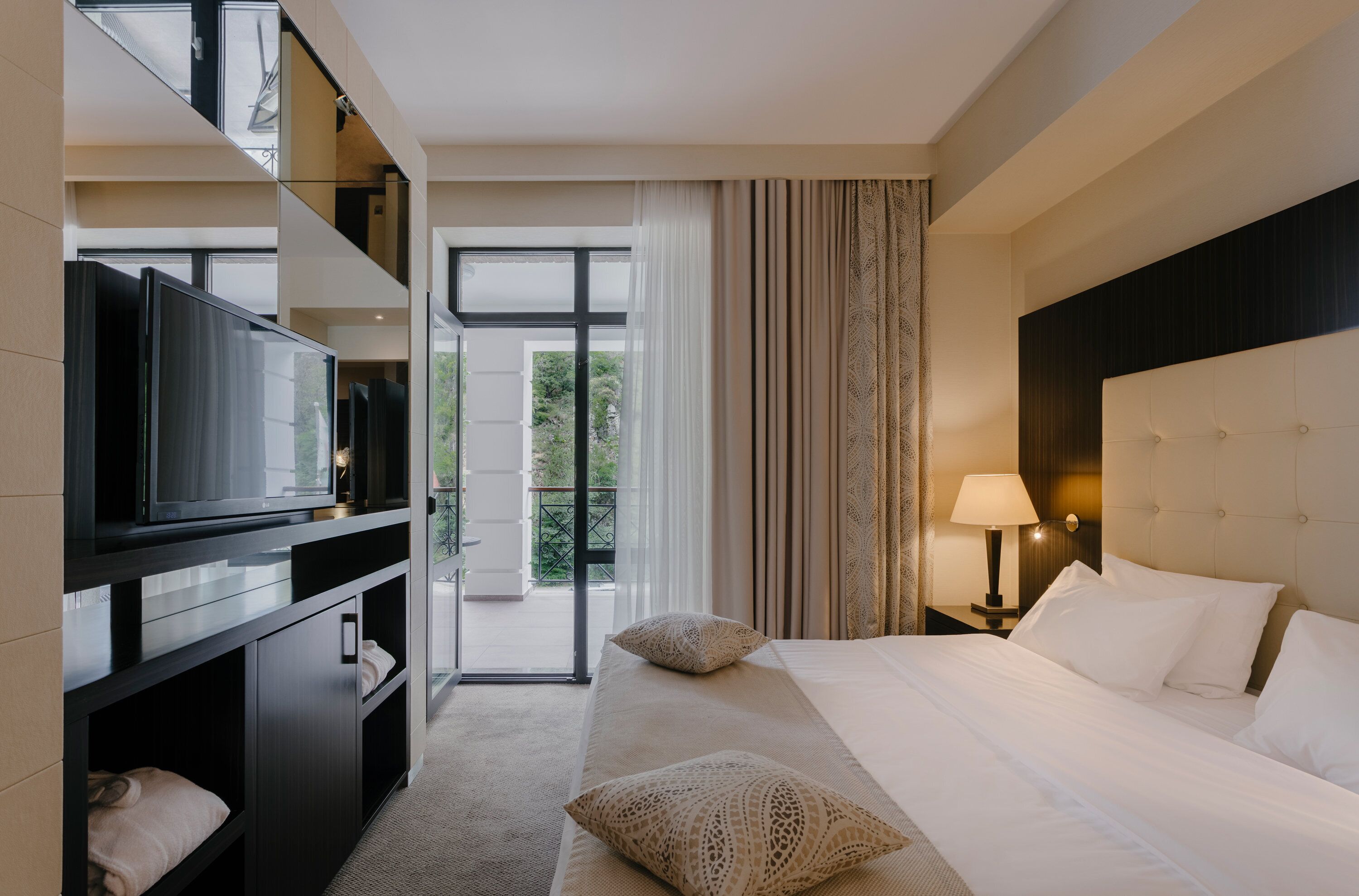 Quarto de hotel com cama, televisão, escrivaninha e vista para o exterior.