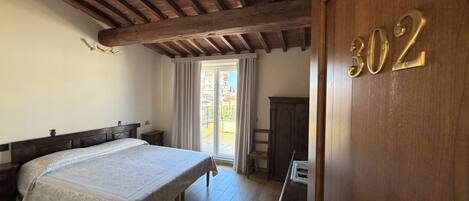 Quarto com teto de madeira, cama com colcha branca, cômoda de madeira e porta com o número 302.