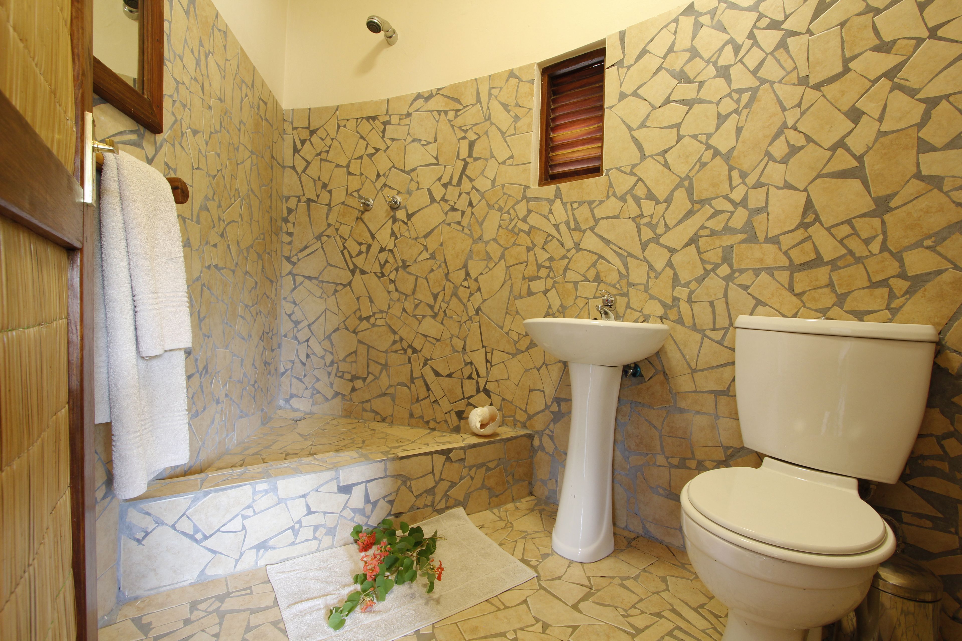 Uma casa de banho com parede em mosaico de pedra, uma pia branca e uma sanita.
