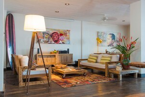 Uma sala de estar acolhedora com um sofá de madeira, uma luminária de chão, uma mesa de centro e uma prancha de surf encostada na parede.