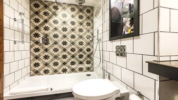 Casa de banho com chuveiro, sanita e lavatório, apresentando um padrão de azulejos geométricos nas paredes.