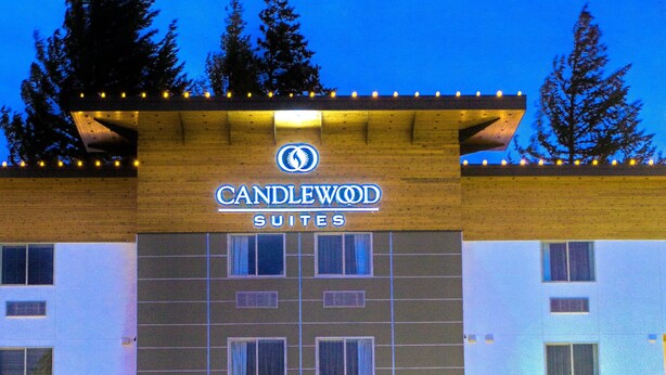 Um hotel com uma placa indicando "CANDLEWOOD SUITES" e uma entrada visível, com pessoas paradas do lado de fora.