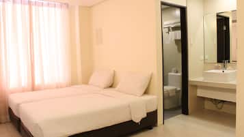 Quarto de hotel com duas camas, banheiro com pia e espelho, e janela com cortinas.