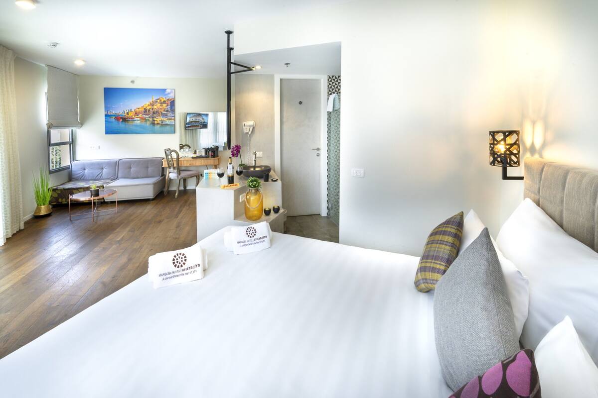 Quarto de hotel com cama, sofá, mesa de jantar e uma pintura na parede.