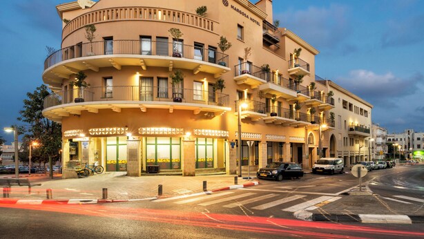 Hotel de vários andares com varandas, entrada no nível da rua e vista da rua com carros e uma faixa de pedestres.