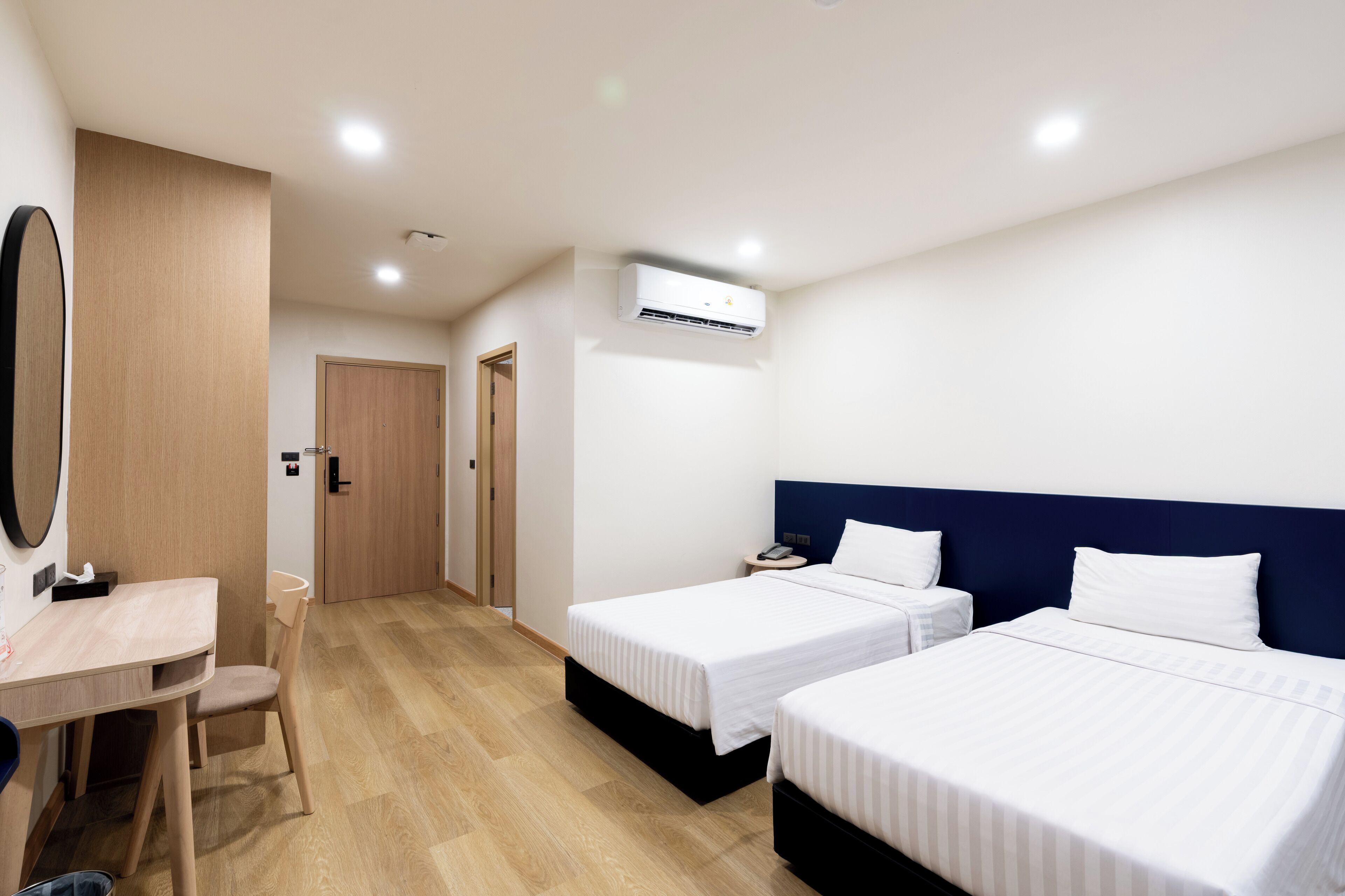Quarto de hotel com duas camas, uma escrivaninha, uma cadeira, um espelho e um ar condicionado.
