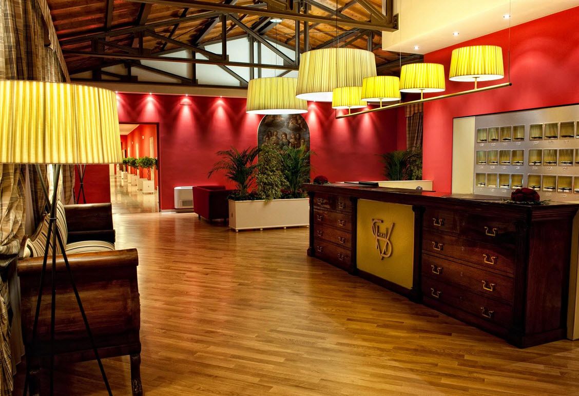 Um hall com piso de madeira, paredes vermelhas e uma mesa de recepção com gavetas.
