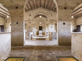 Interior com tetos em arco, paredes de pedra e um corredor central que leva a uma porta.