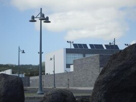 Um edifício moderno com painéis solares no telhado, rodeado por grandes rochas e postes de iluminação pública.