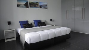 Quarto moderno com cama grande, duas mesas de cabeceira, guarda-roupa e três quadros de paisagens na parede.