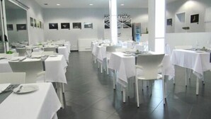Uma sala de jantar ampla com várias mesas preparadas para refeições, cadeiras brancas e design de interiores moderno.