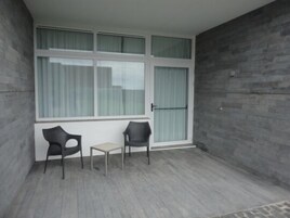 Varanda com vista para um prédio, duas cadeiras e uma mesa pequena.