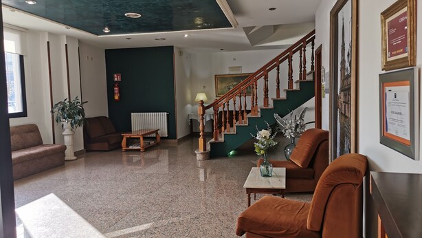 Um saguão de hotel com uma escadaria de madeira, um balcão de recepção e áreas de estar.