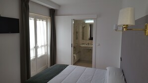 Quarto de hotel com cama, banheiro com pia e espelho, e janela com cortinas.