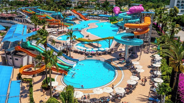 Parque aquático com várias piscinas e toboáguas, cercado por espreguiçadeiras e guarda-sóis.