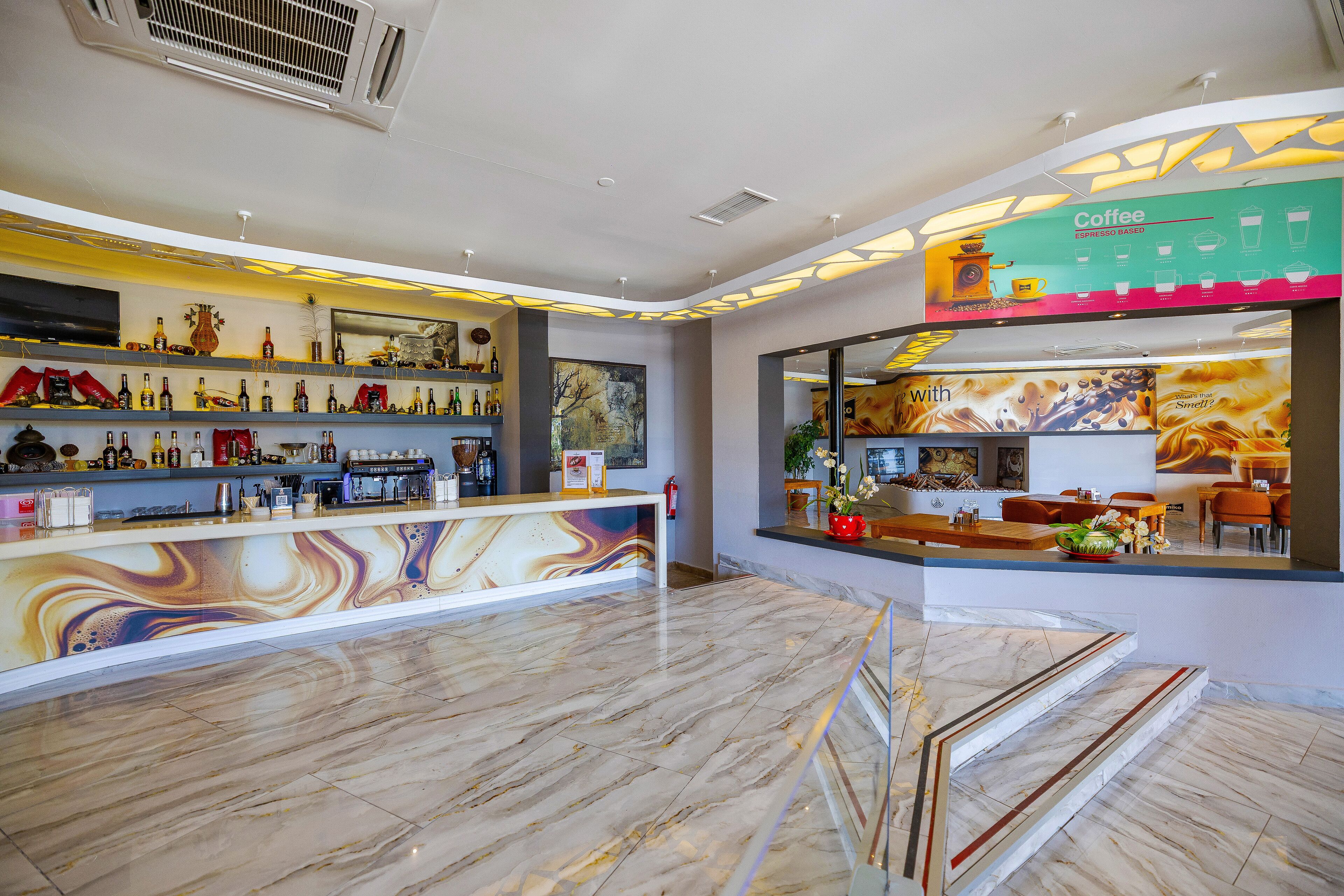 Uma área de bar moderna com piso de mármore, um canto de café e diversas garrafas e copos em prateleiras.