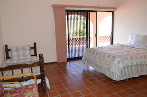 Quarto com cama, uma cadeira e porta de correr para uma varanda.