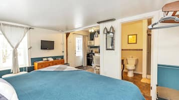 Quarto com cama grande, penteadeira, televisão e banheiro visível por uma porta aberta.