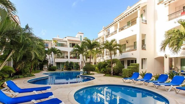 Uma área de piscina com espreguiçadeiras azuis e palmeiras.