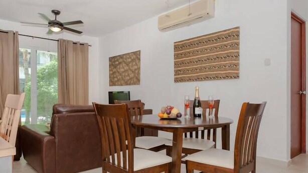 Uma sala de jantar com uma mesa de madeira redonda, quatro cadeiras de madeira, um sofá marrom e um ventilador de teto.