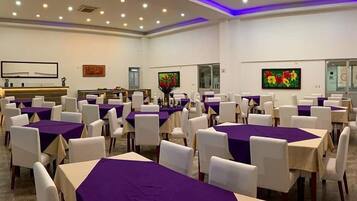 Uma sala de conferências com várias mesas e cadeiras, paredes brancas e luminárias no teto.