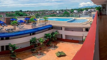 Área de piscina no terraço com espreguiçadeiras e guarda-sóis, cercada por plantas em vasos e vista para a cidade.