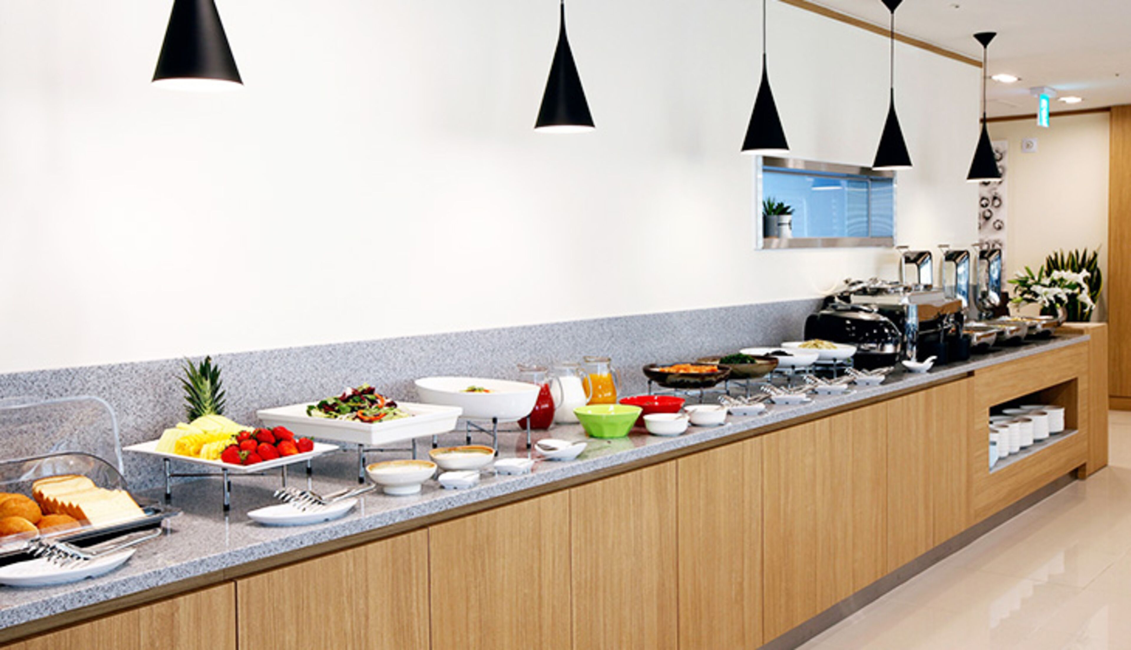 Uma cozinha moderna com um balcão comprido, diversos alimentos e luminárias pendentes pretas.