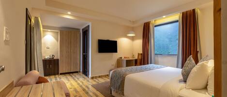 Quarto de hotel com cama, escrivaninha, cadeira, televisão e janela.