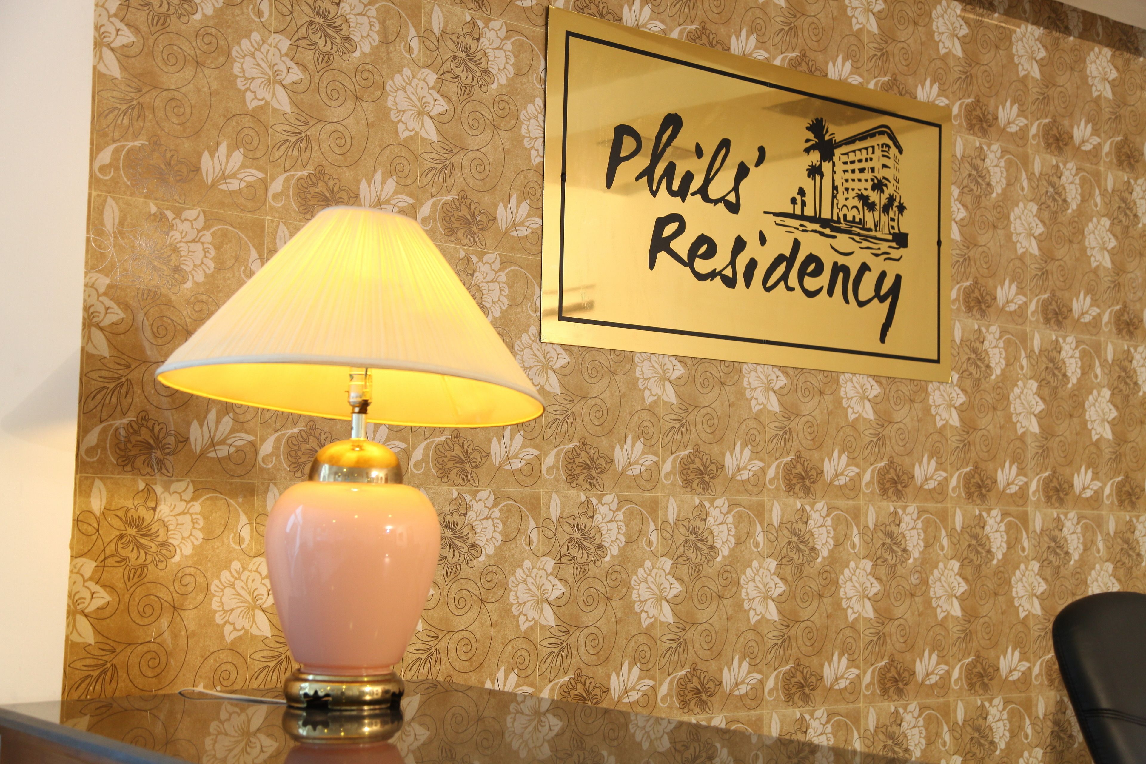 Um abajur sobre uma bancada com papel de parede floral e uma placa que diz 'Phil's Residency'.