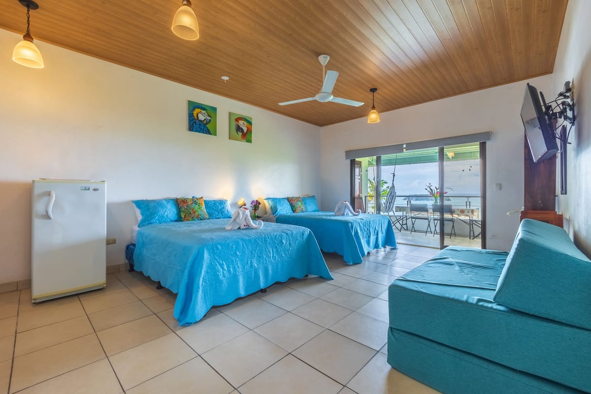 Quarto com duas camas, um sofá, um ventilador de teto e uma geladeira.