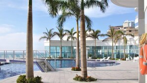 Área de piscina com palmeiras, espreguiçadeiras e um flutuador.