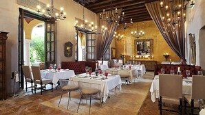 Um restaurante com várias mesas e cadeiras, lustres e vista para o exterior.