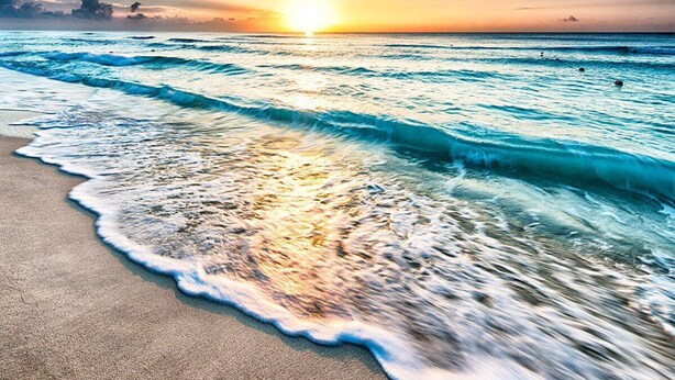 Uma praia com ondas e um pôr do sol.
