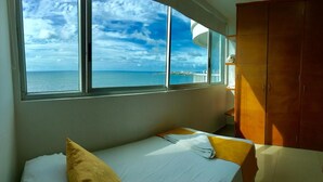 Quarto com cama, guarda-roupa e janela com vista para o mar e uma ilha ao longe.