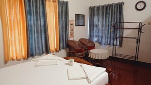 Quarto com cama, uma mesa pequena, duas cadeiras, um cabideiro e cortinas.