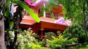 Uma casa com telhado vermelho, rodeada por vegetação exuberante e diversas plantas.