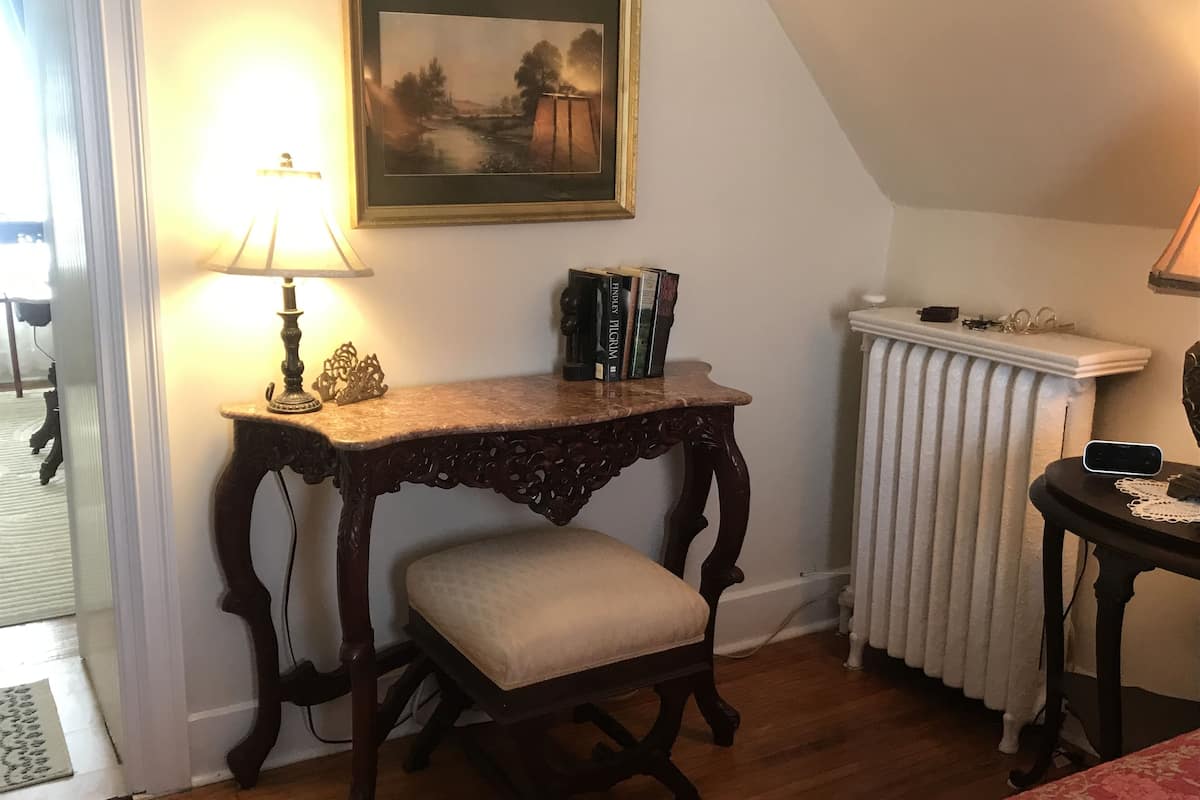 Quarto com escrivaninha de madeira, cadeira, radiador e quadro pendurado na parede.
