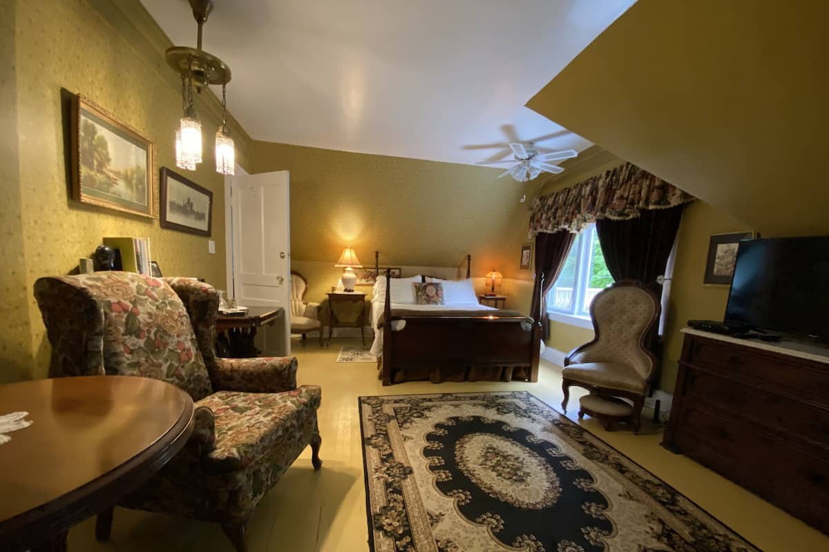 Uma sala de estar aconchegante com uma mesa redonda de madeira, poltronas florais, um tapete grande, uma televisão e um ventilador de teto.