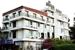 Um hotel com vários andares, varandas, aparelhos de ar condicionado e placas indicando o Banco Central da Índia e um caixa eletrônico 24 horas.