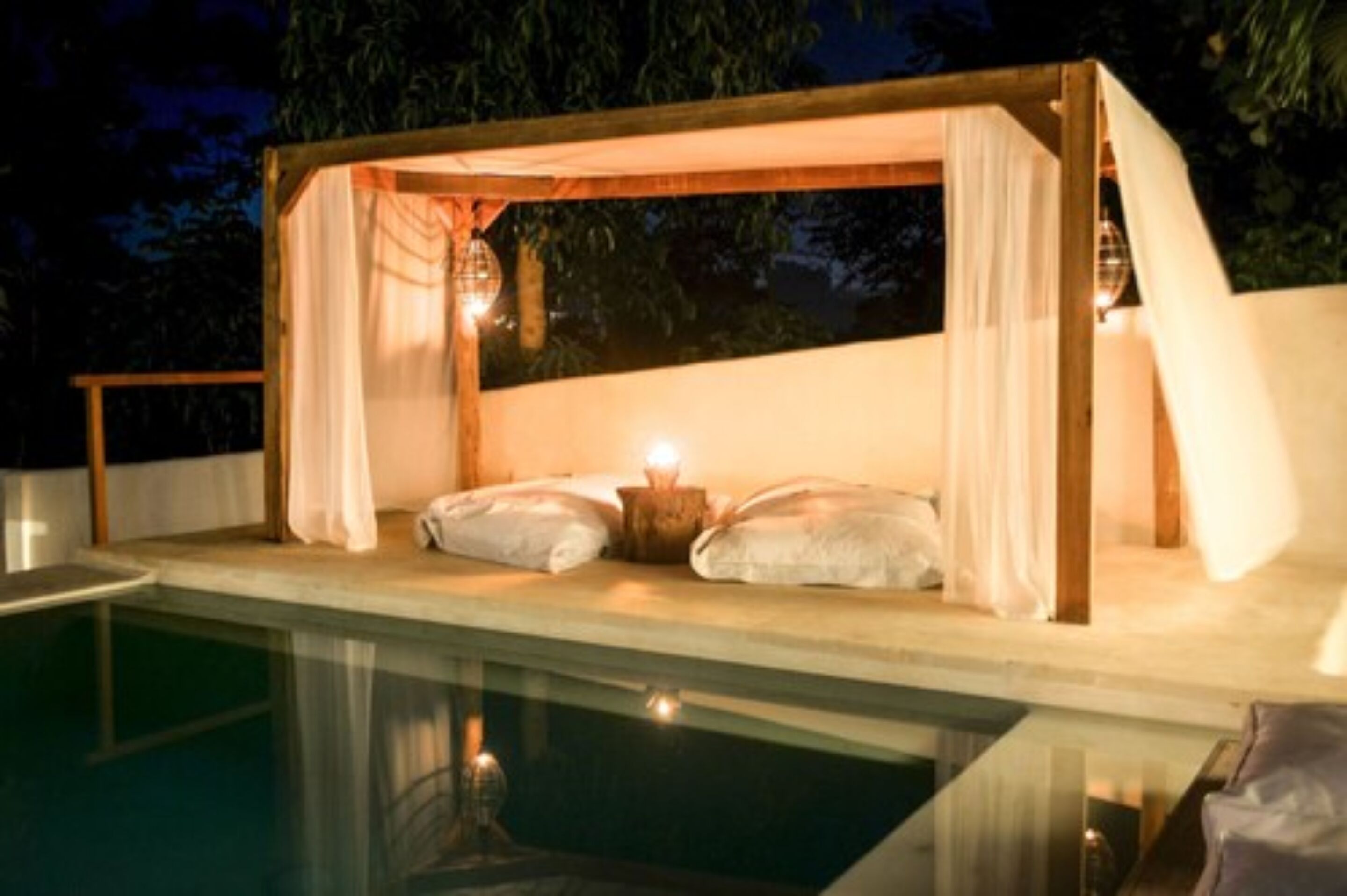 Quarto junto à piscina com dossel, almofadas e abajur.