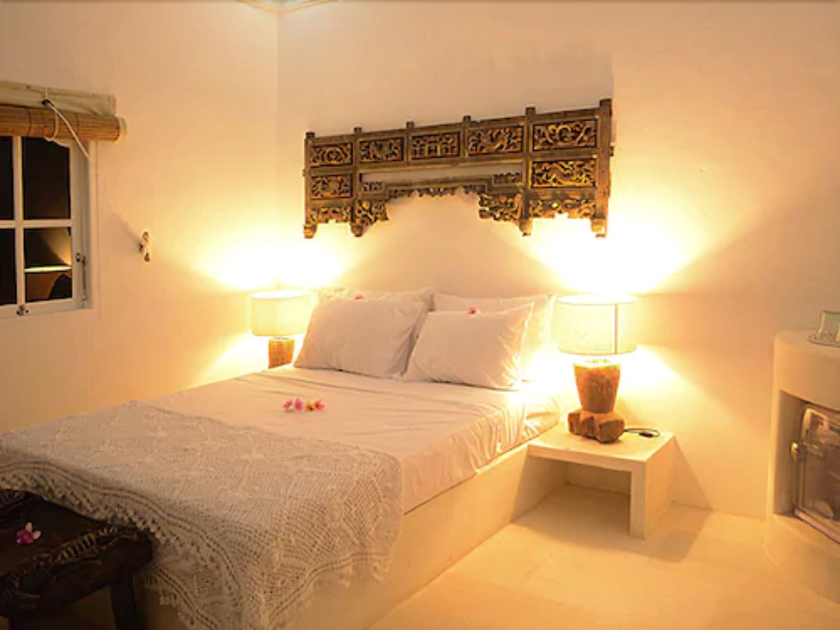 Quarto com cama, duas luminárias de cabeceira, um objeto decorativo na parede e uma janela com cortina.