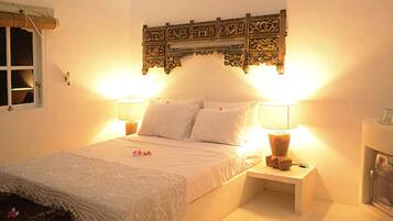 Quarto com cama, duas luminárias de cabeceira, um objeto decorativo na parede e uma janela com cortina.
