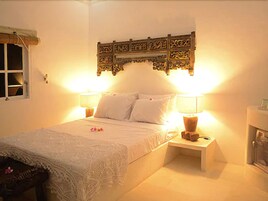 Quarto com cama, duas luminárias de cabeceira, um objeto decorativo na parede e uma janela com cortina.