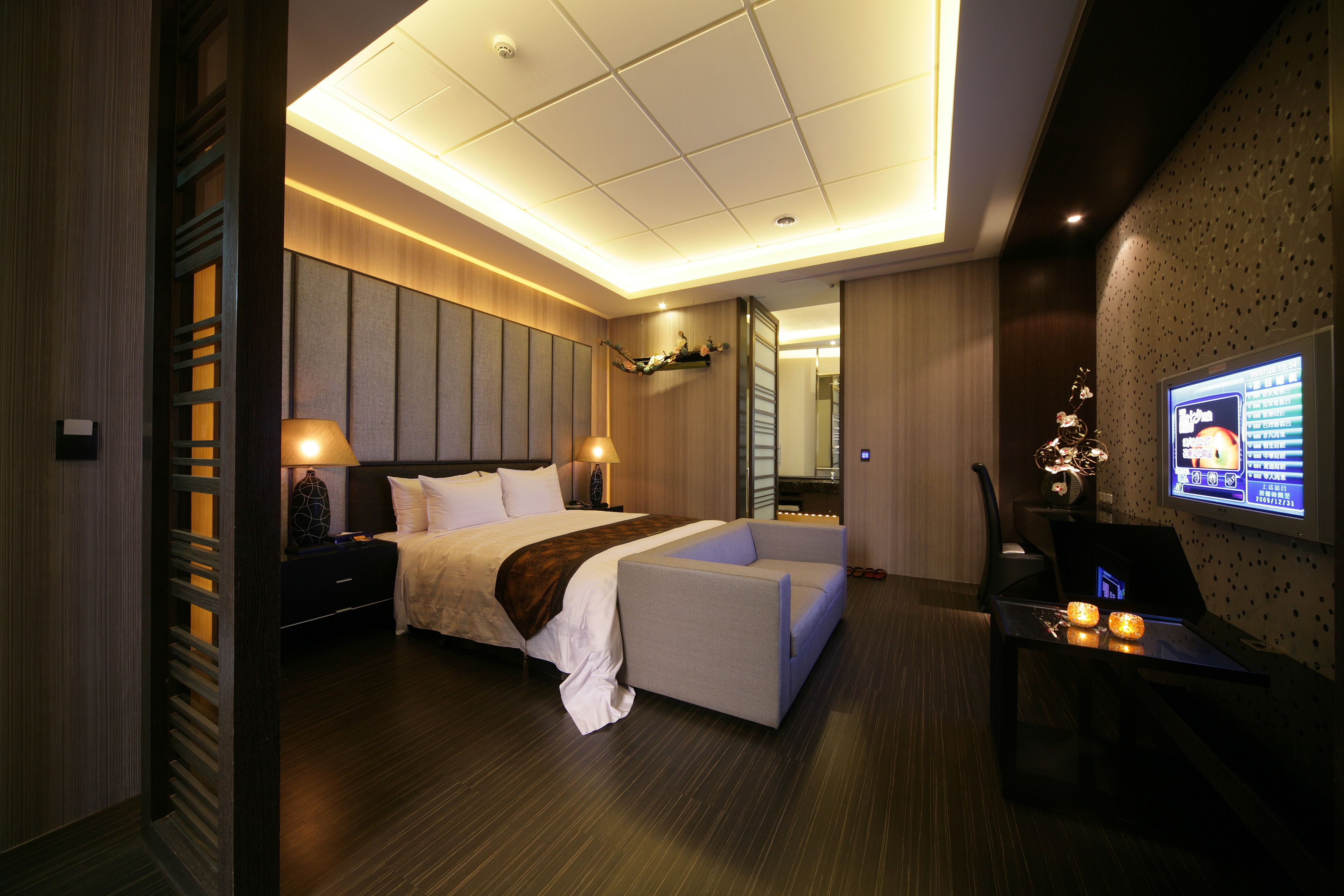 Quarto de hotel moderno com uma cama grande, um sofá, uma escrivaninha e uma televisão.