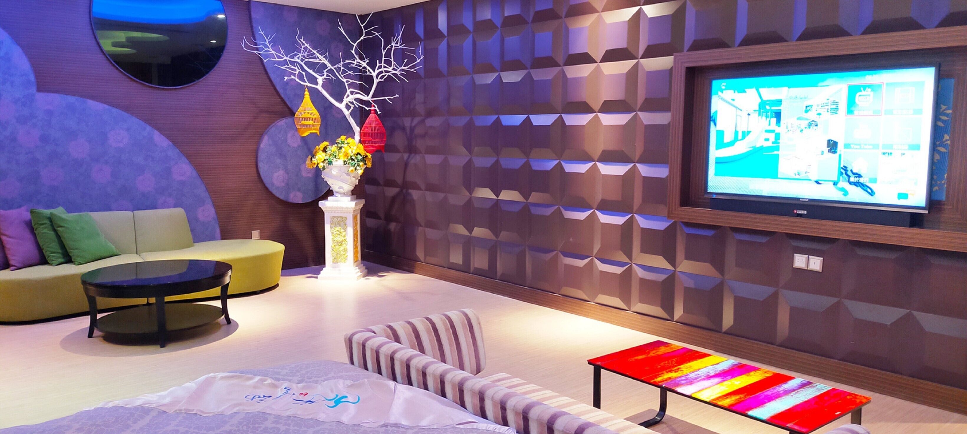 Uma sala de estar moderna com um sofá, uma mesa de centro redonda, uma poltrona listrada, uma mesa lateral colorida, uma árvore decorativa e uma televisão na parede.