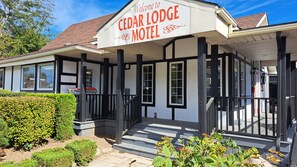 Um motel Cedar Lodge com fachada branca, detalhes em preto e uma placa convidativa.