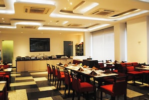 Uma sala de jantar moderna com piso xadrez, várias mesas e cadeiras estofadas vermelhas.