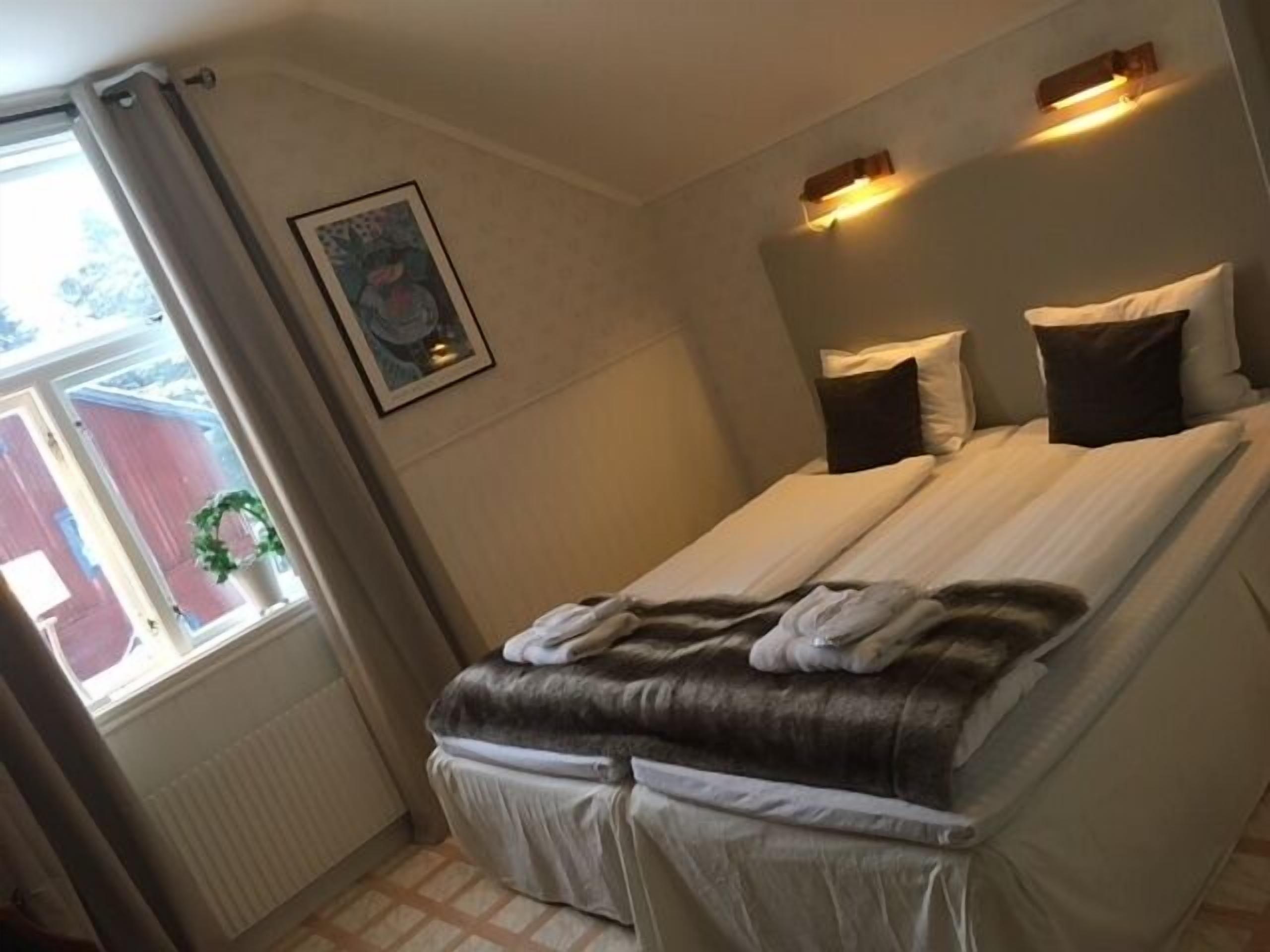 Quarto com cama, janela com cortinas, radiador e luminária fixada na parede.