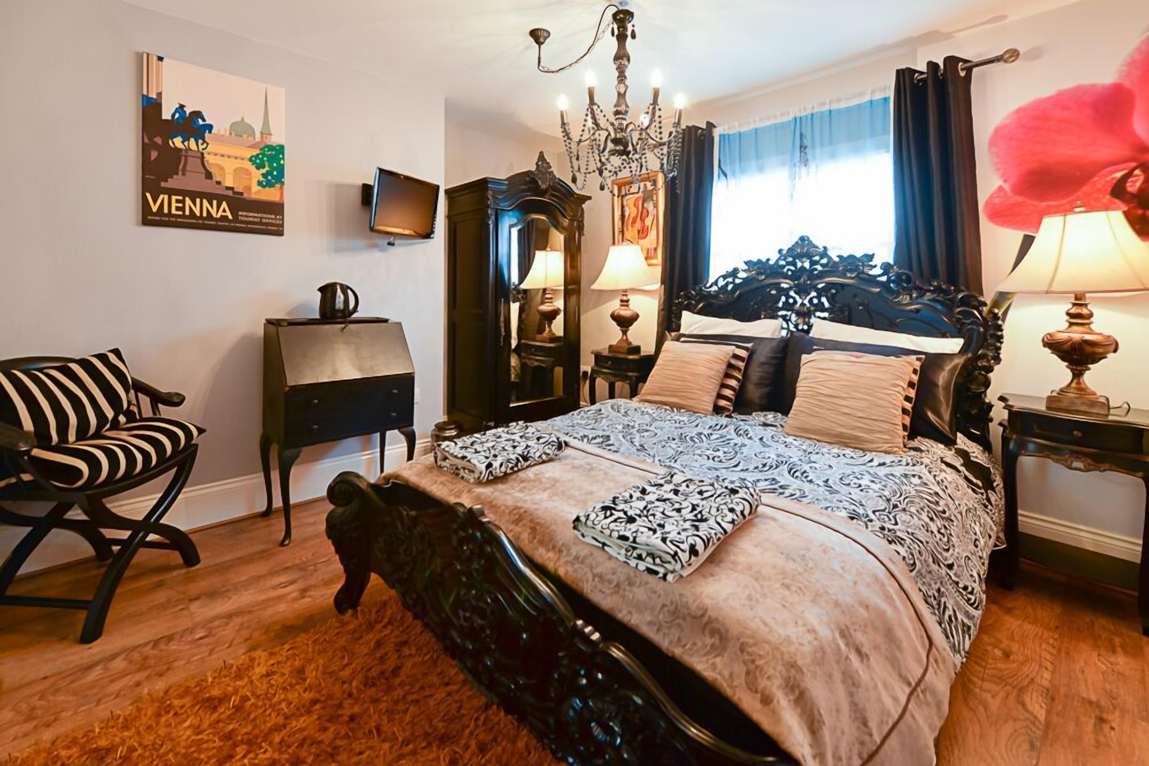 Quarto de hotel com uma cama grande, uma cadeira, uma escrivaninha e um candelabro.