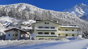Um hotel de vários andares com varandas, rodeado por montanhas e árvores cobertas de neve.
